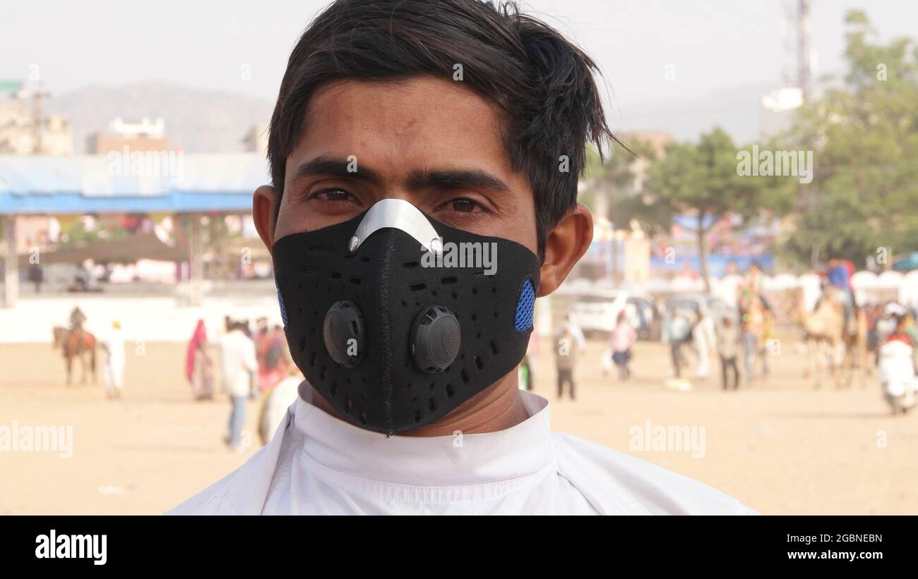 Young Indian man in traditional clothes and facial mask walking outdoor ...