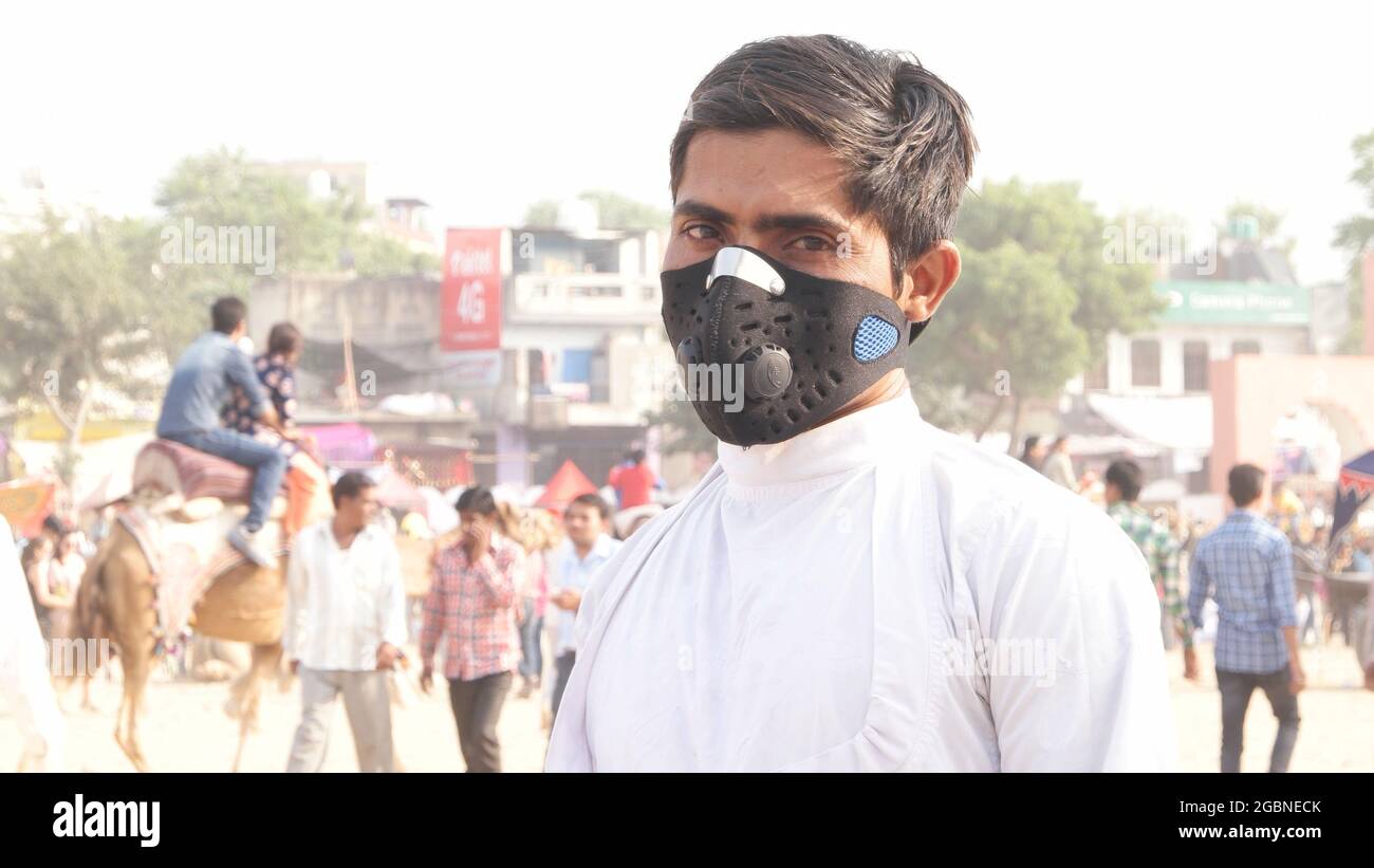 Young Indian man in traditional clothes and facial mask walking outdoor ...