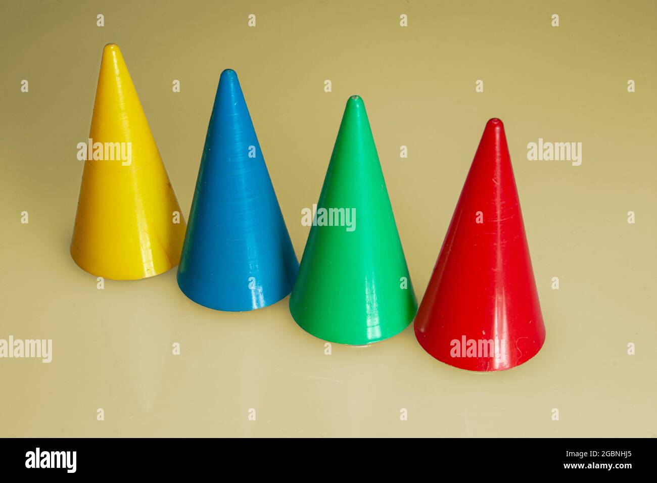 four different colored cone shaped game pieces in a row against ocher ...