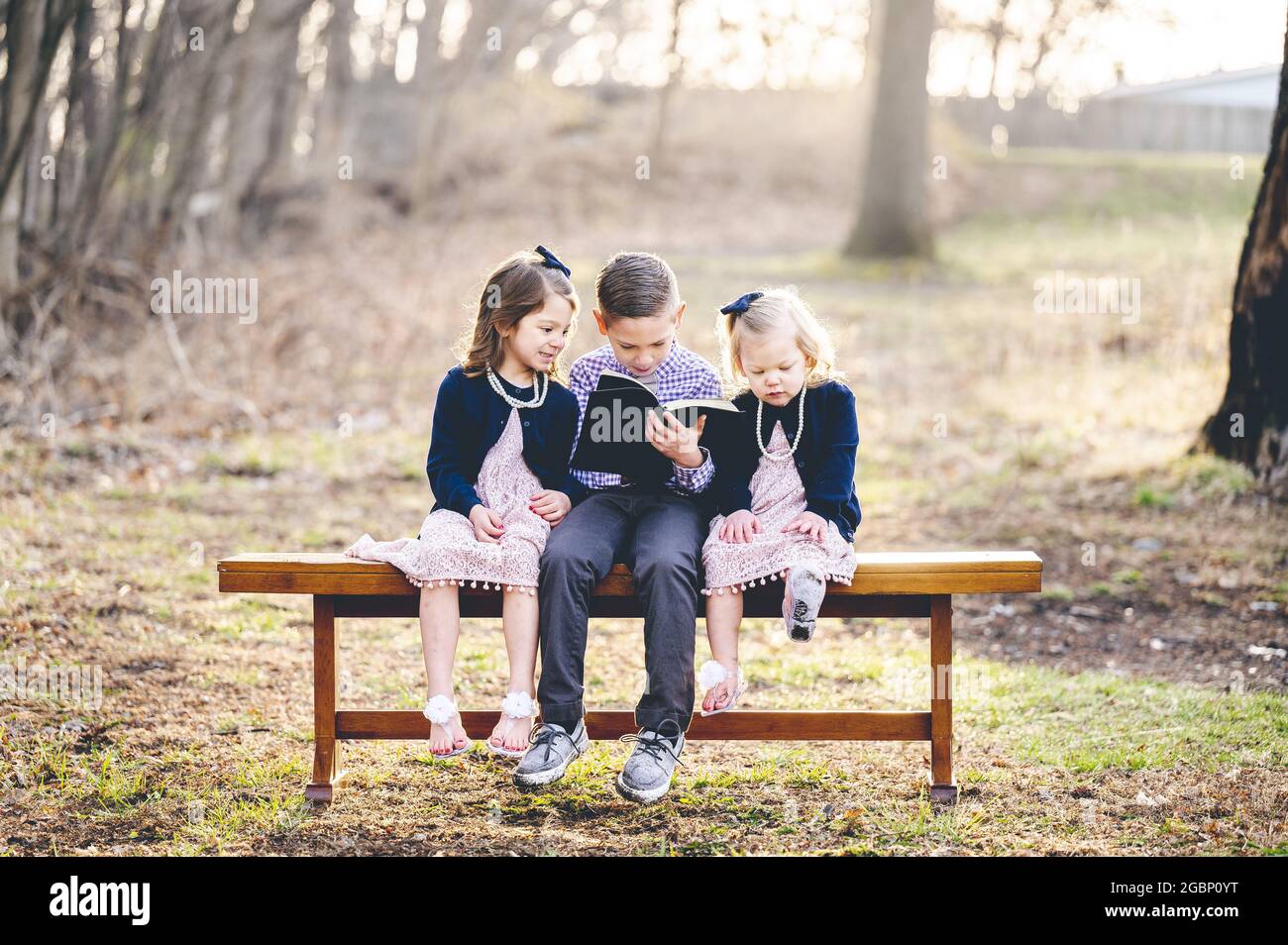 Scenic view of kids sitting on the bench and reading the Bible Stock ...