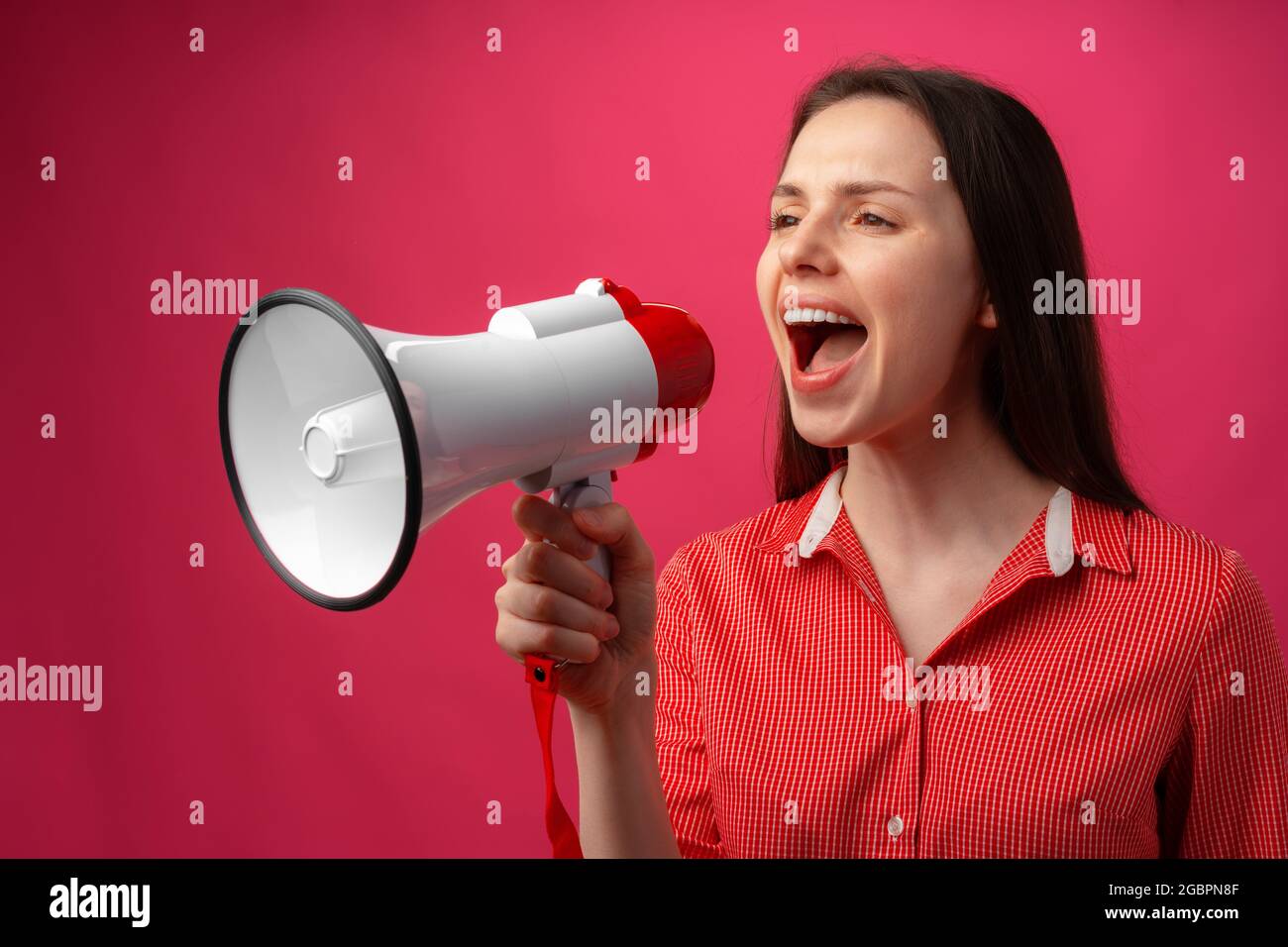 Young brunette woman shouting in megaphone against pink background ...