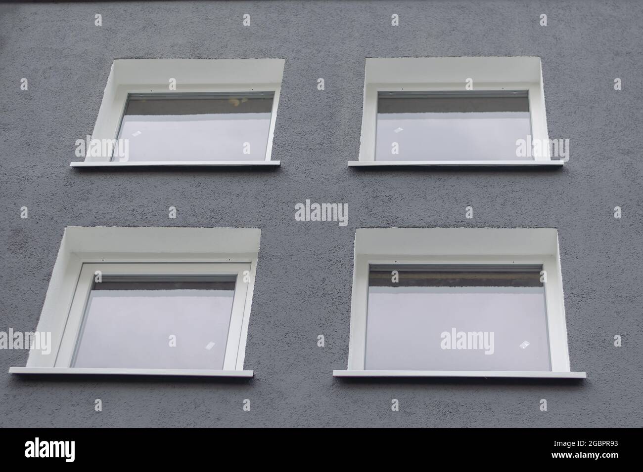 Dark gray exterior wall with white windows. Four square windows on the ...