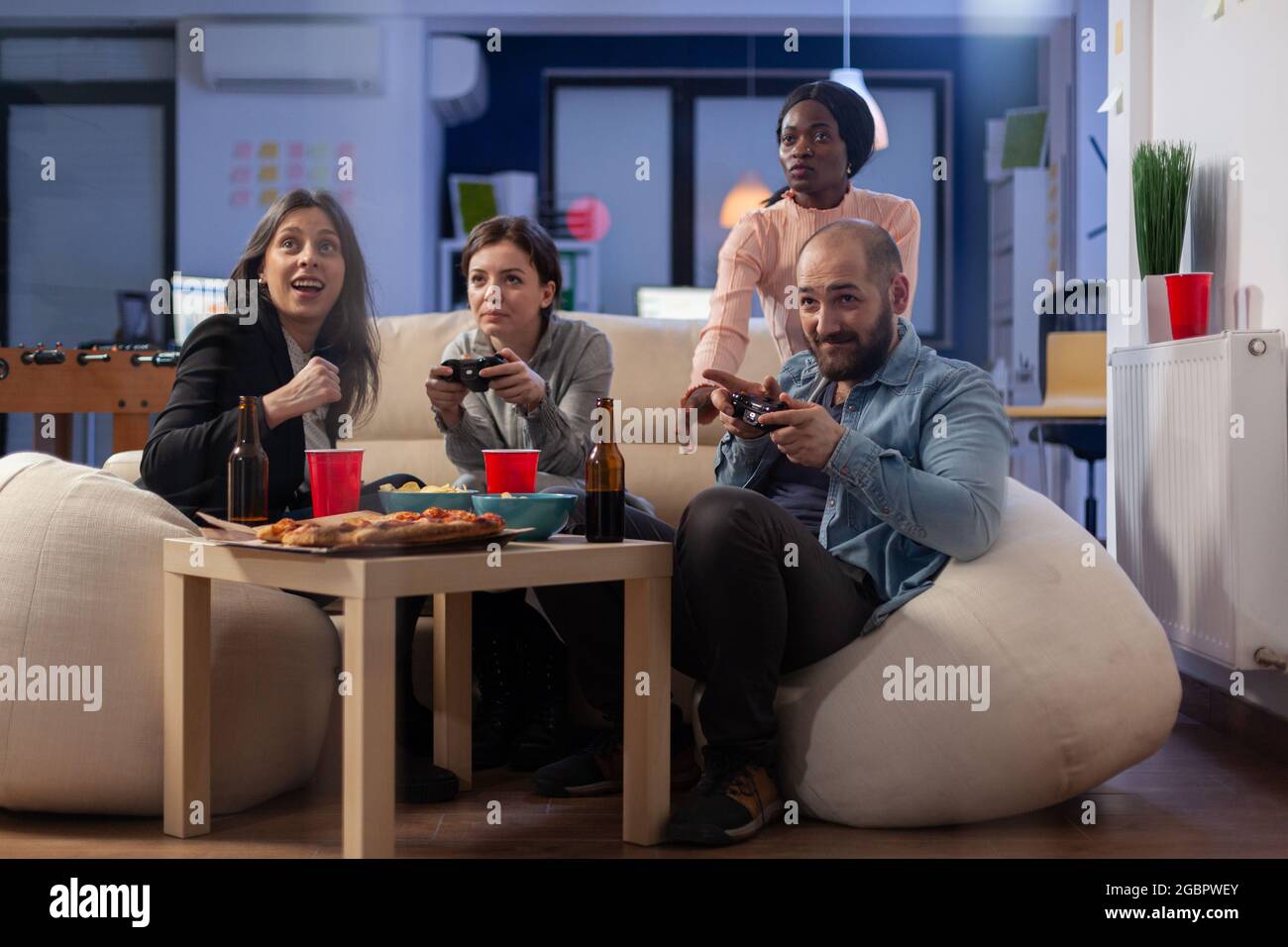 Multi ethnic group of coworkers play game on console while holding ...