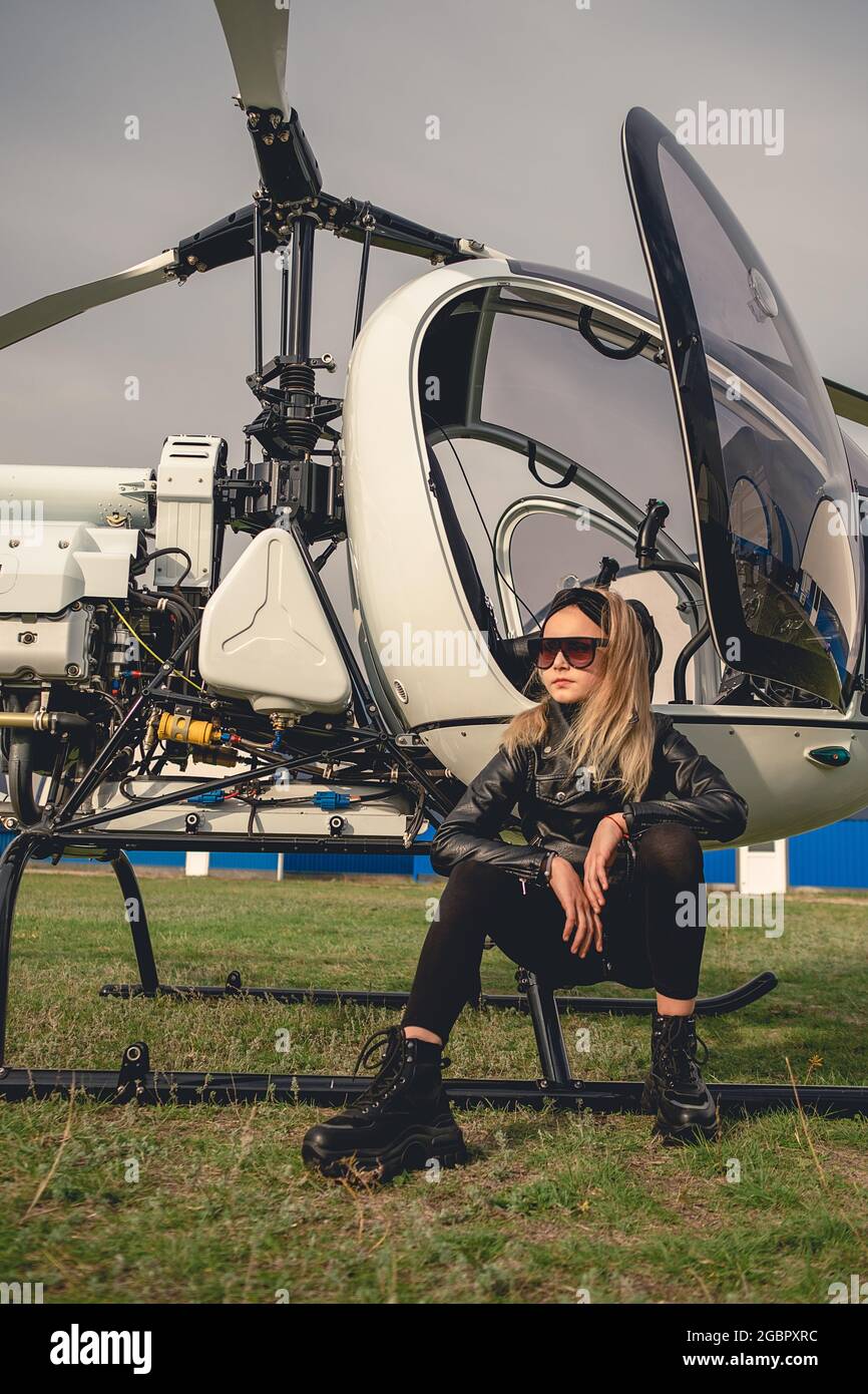 Confident blonde tween girl sitting on landing skids of helicopter ...