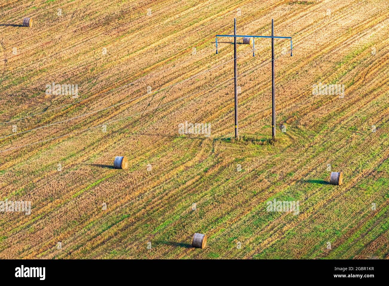 Power line pylon at a stubble field with round bales Stock Photo - Alamy