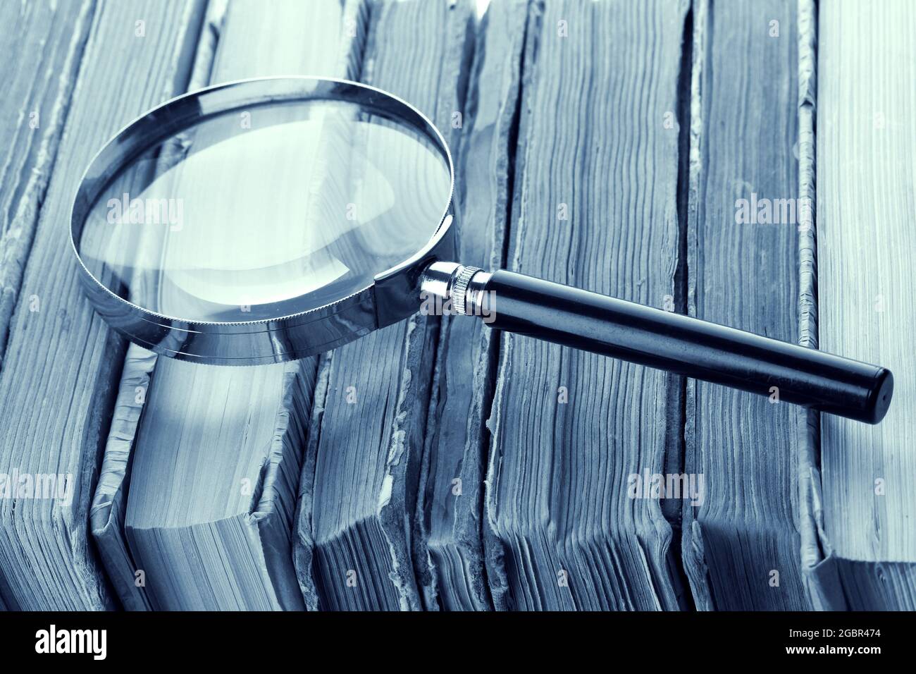 Magnifying glass over the stack of books in grey light Stock Photo - Alamy