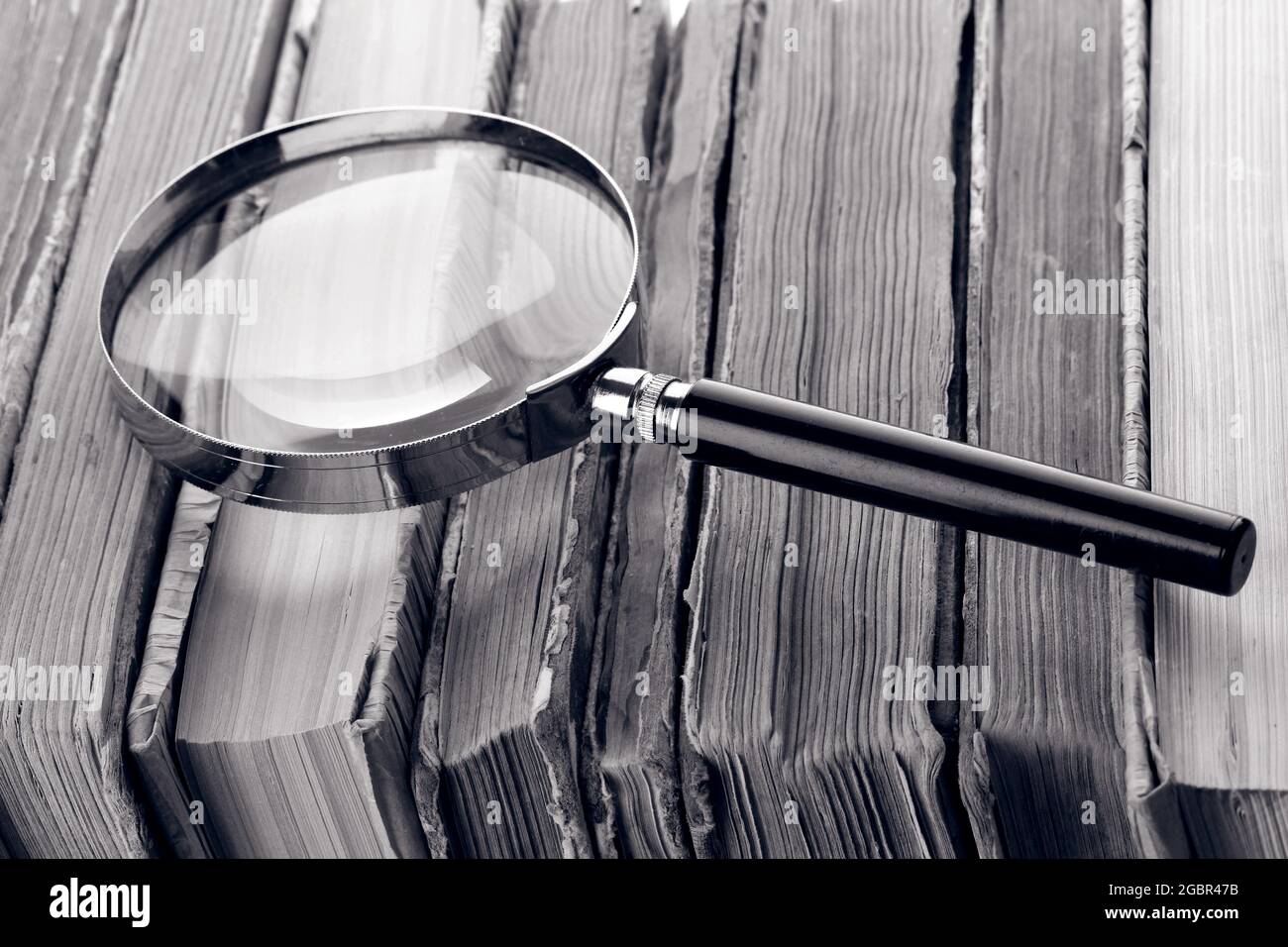 Magnifying glass over the stack of books in grey light Stock Photo - Alamy