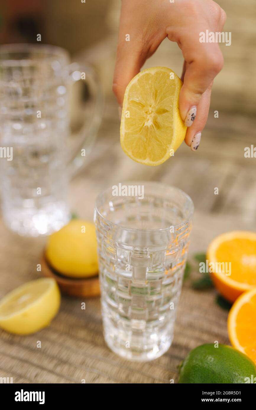 Home made healthy vitamin-fortified water. Woman squeezes lemon juice ...