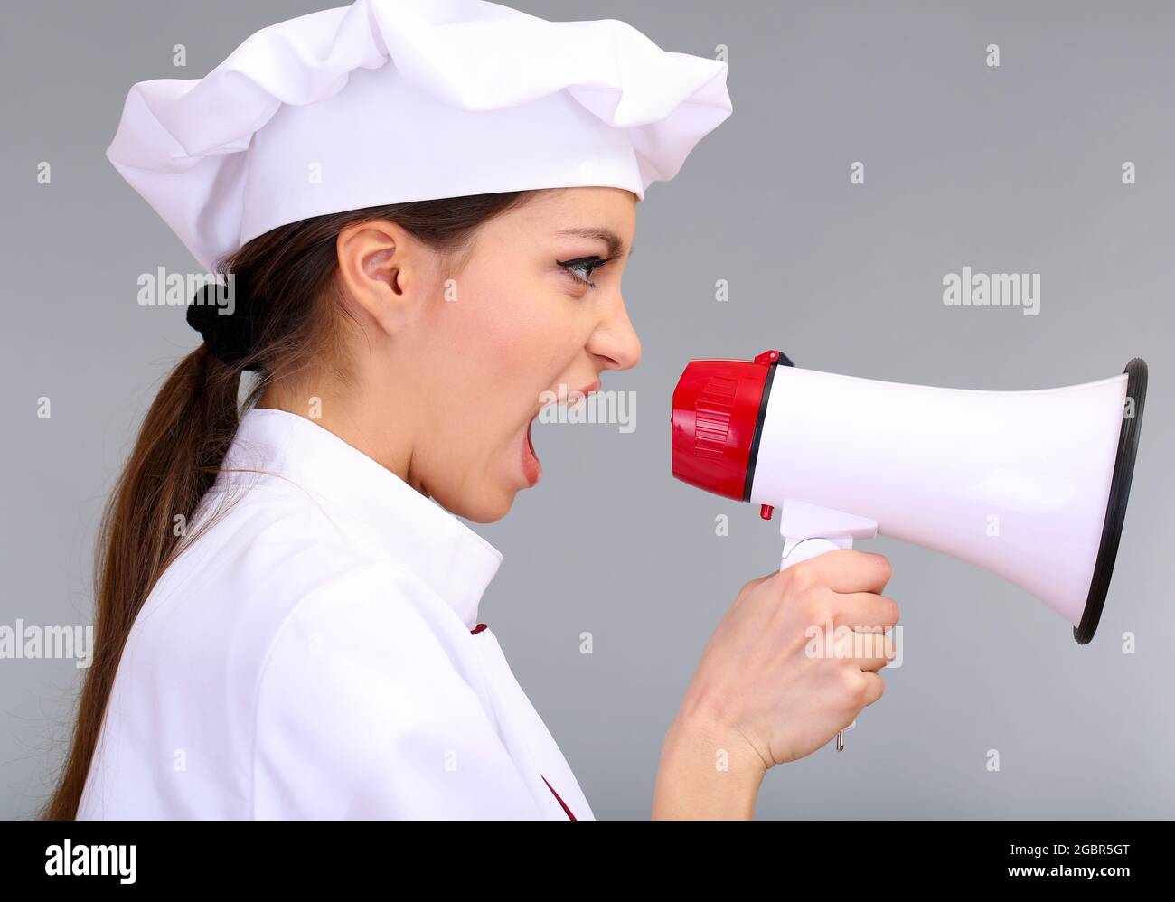 Portrait of young woman chef with megaphone on grey background Stock ...
