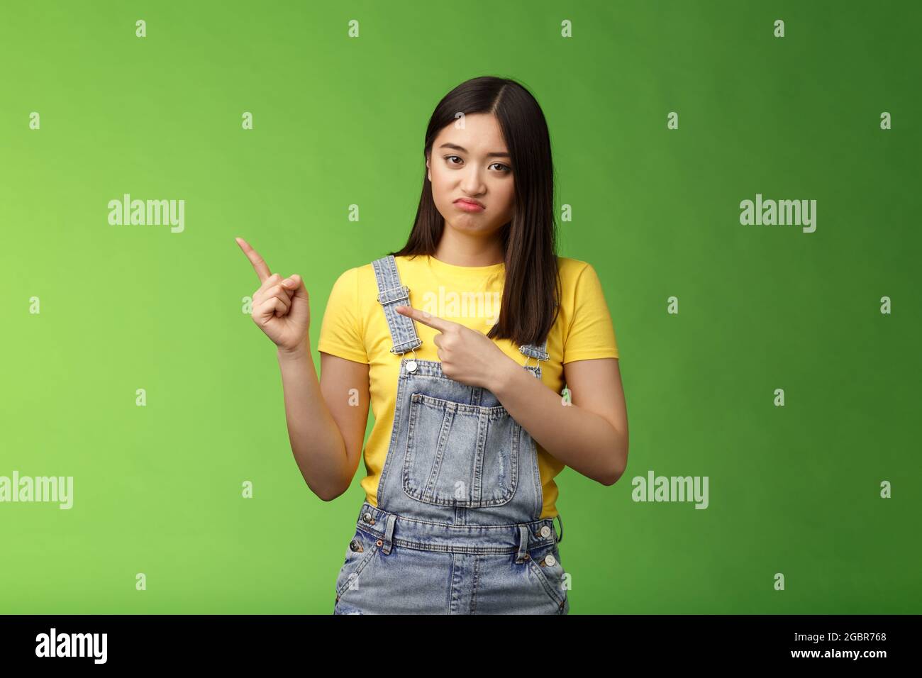 Disappointed uninterested asian gloomy girl pointing fingers left ...