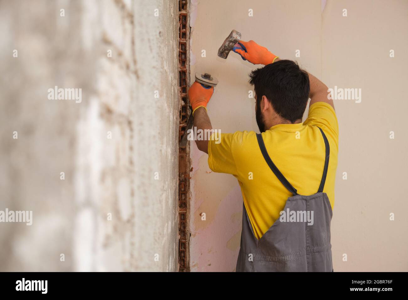 Young builder breaking up a house wall with a hammer and a chisel Stock ...