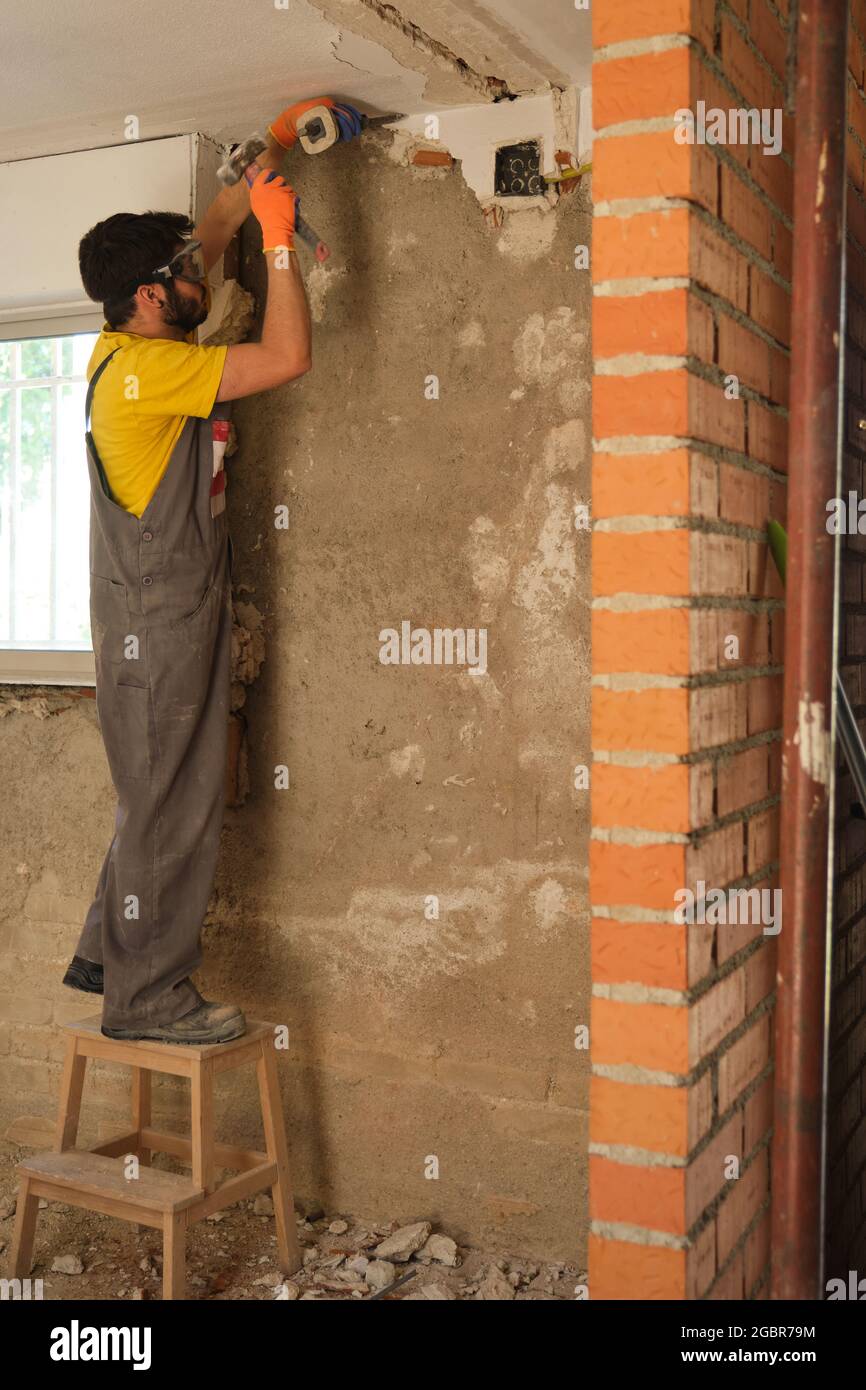 Young builder breaking up a house wall with a hammer and a chisel Stock ...