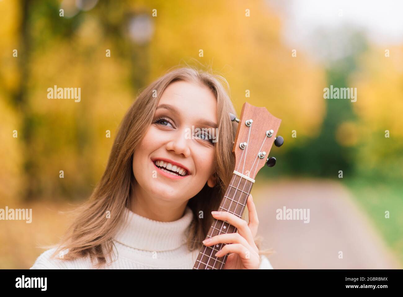 Beautiful woman playing ukulele guitar at outdoor in an autumn forest ...
