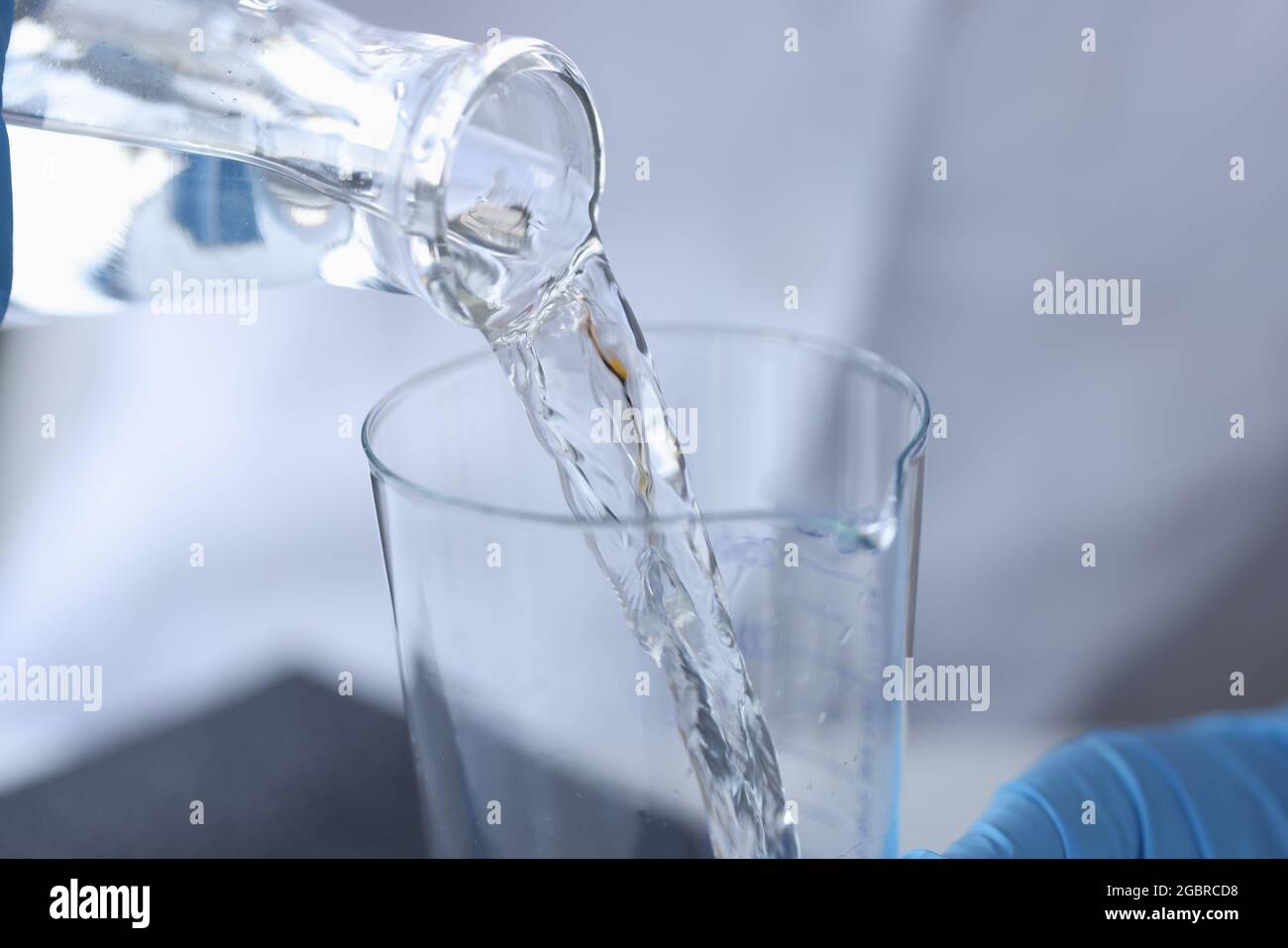 Scientist chemist pouring water from transparent bottle into flask in ...