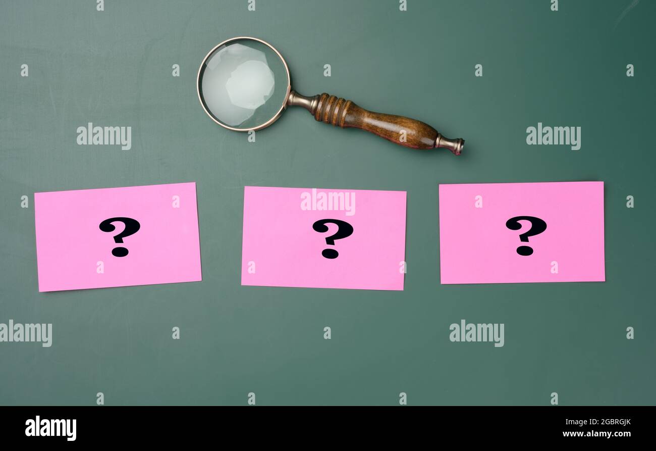 wooden magnifying glass and white chalk drawn question marks on a green ...