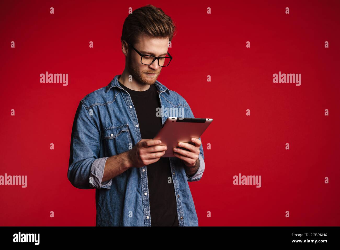 Calm young man in casual clothes standing over red wall background ...