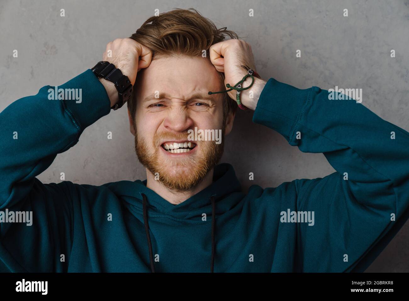 White ginger man with beard frowning while holding his head isolated ...
