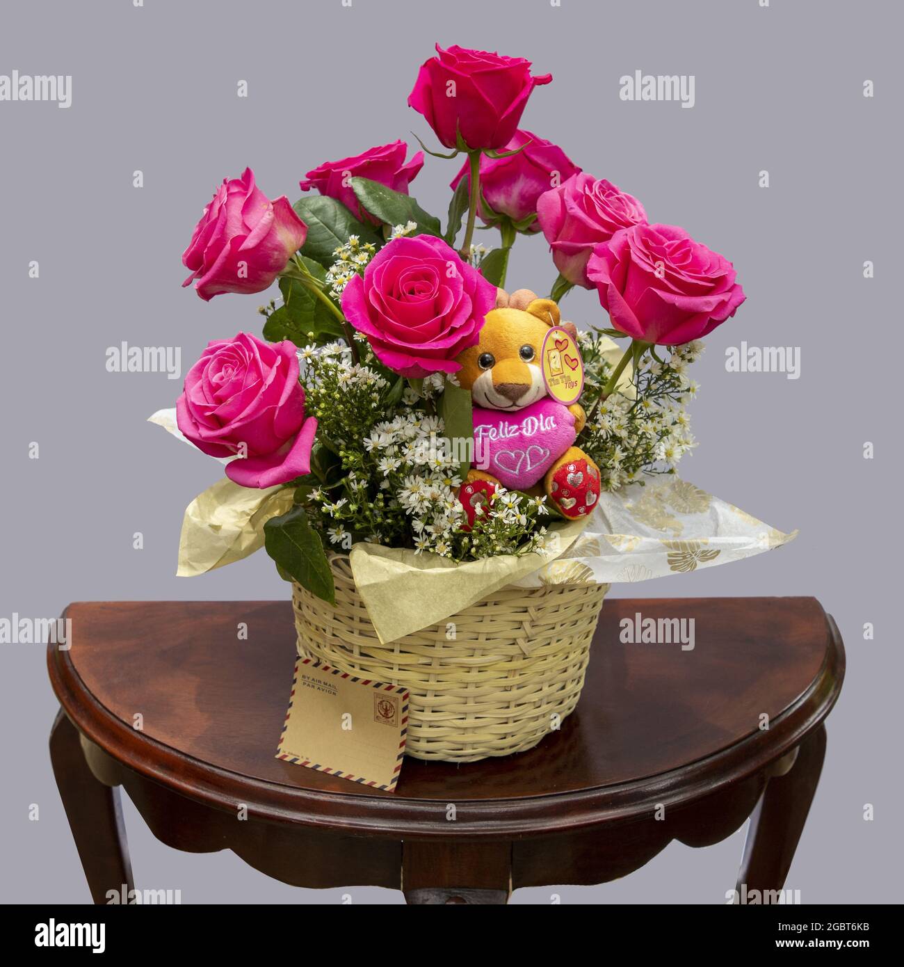 Basket full of pink roses, a toy and a champagne bottle on a wooden ...