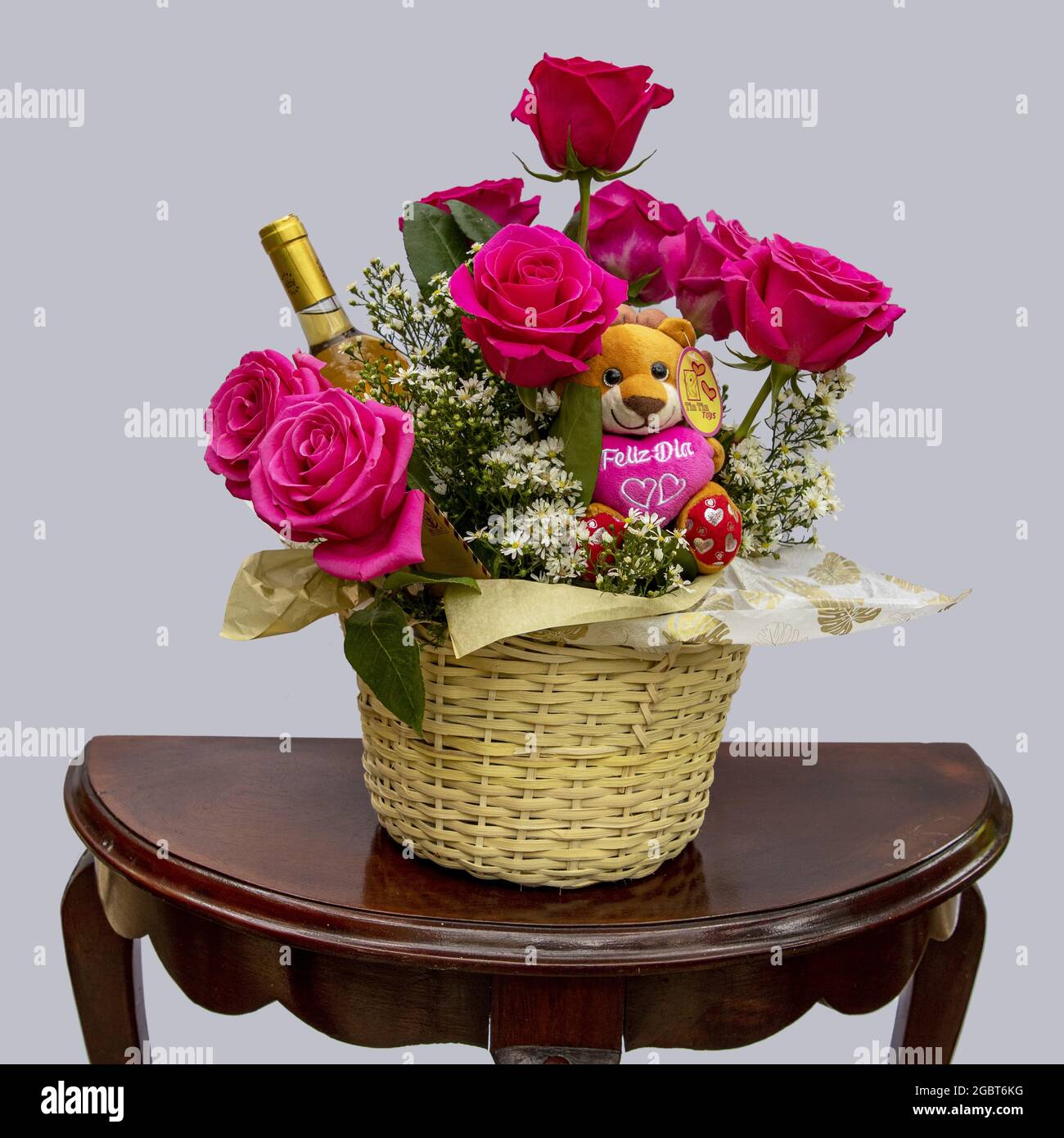 Basket full of pink roses, a toy and a champagne bottle on a wooden ...