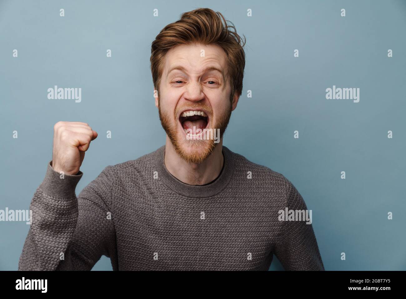White ginger man with beard screaming while making winner gesture ...