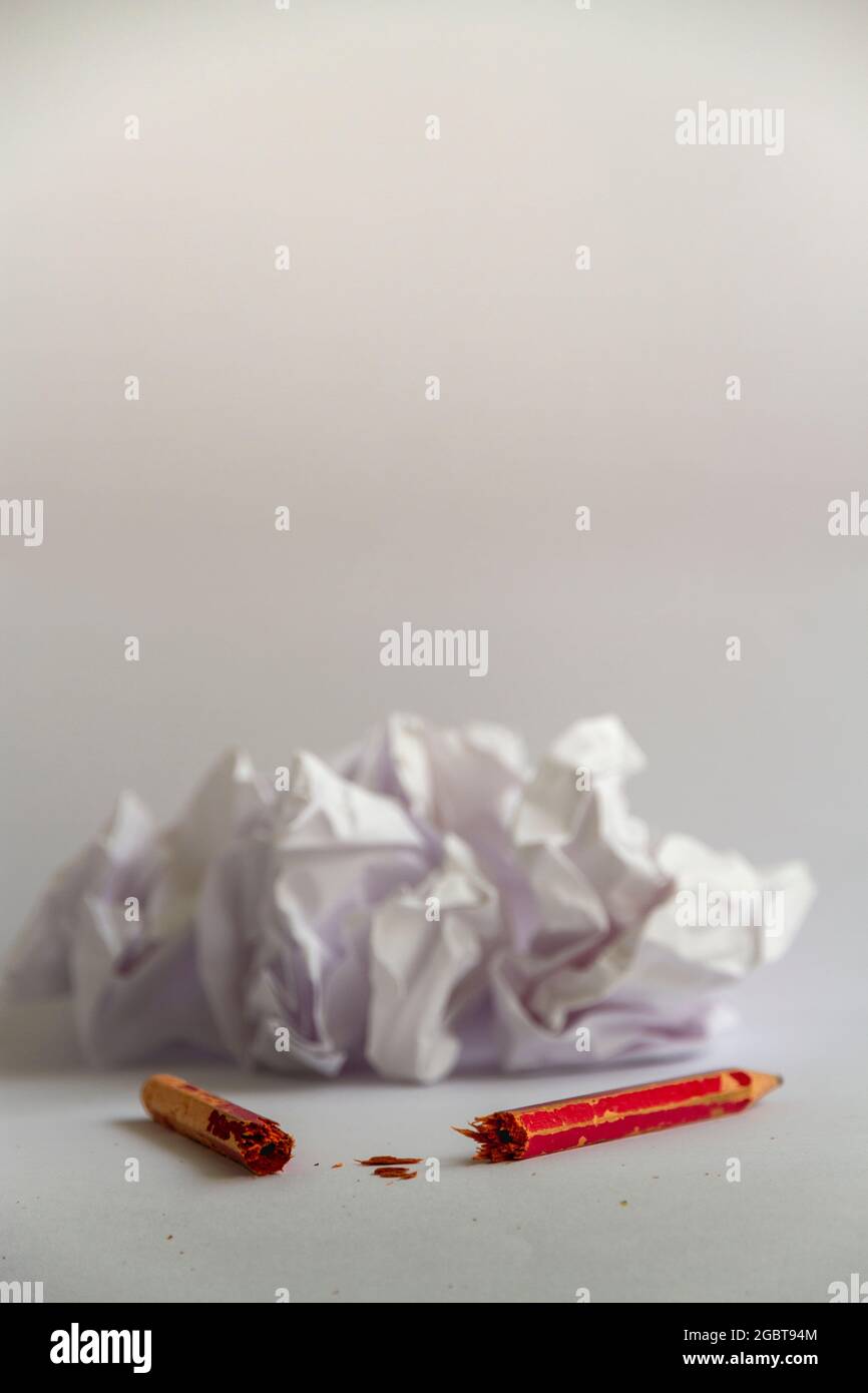 A broken and chewed pencil in front of a pile of screwed up paper ...