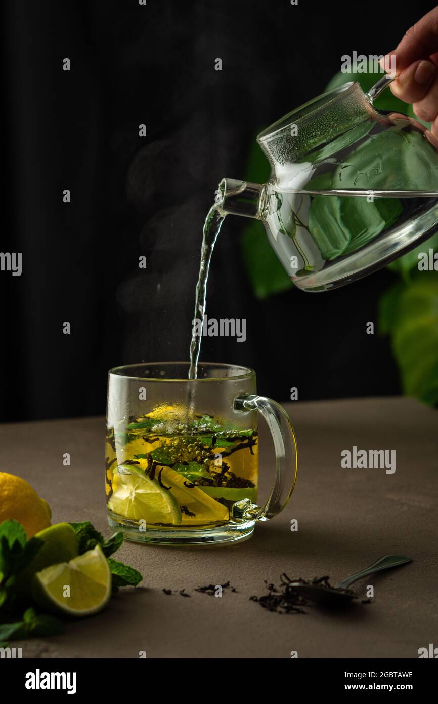 Woman pours boiling water from a teapot into a mug with mint, lemon ...