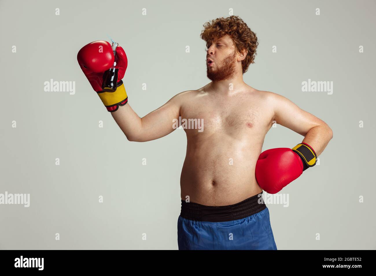 Funny red-headed man in blue boxing shorts and gloves isolated on gray ...