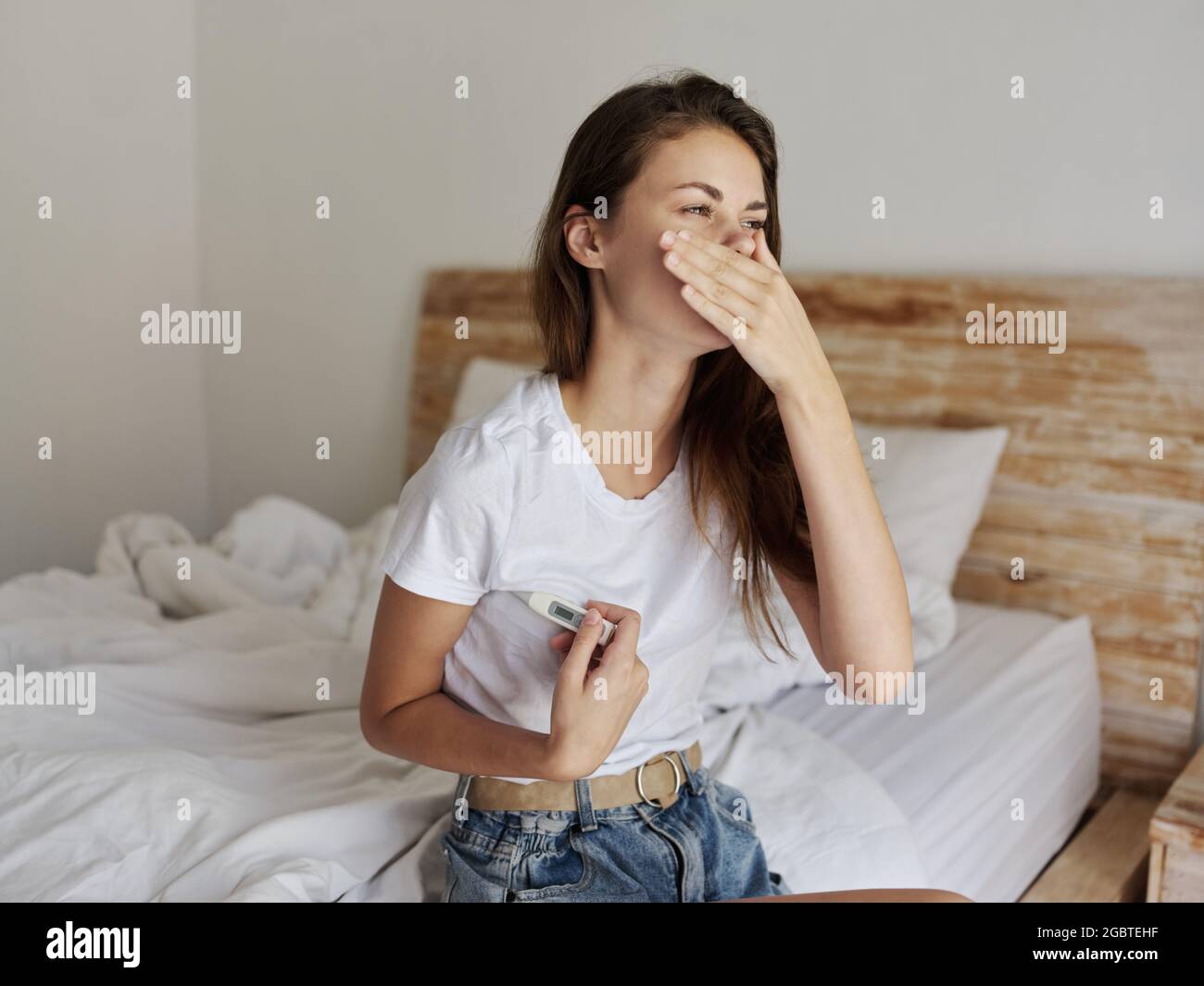 woman with a thermometer under her arm covers her face with her hand ...