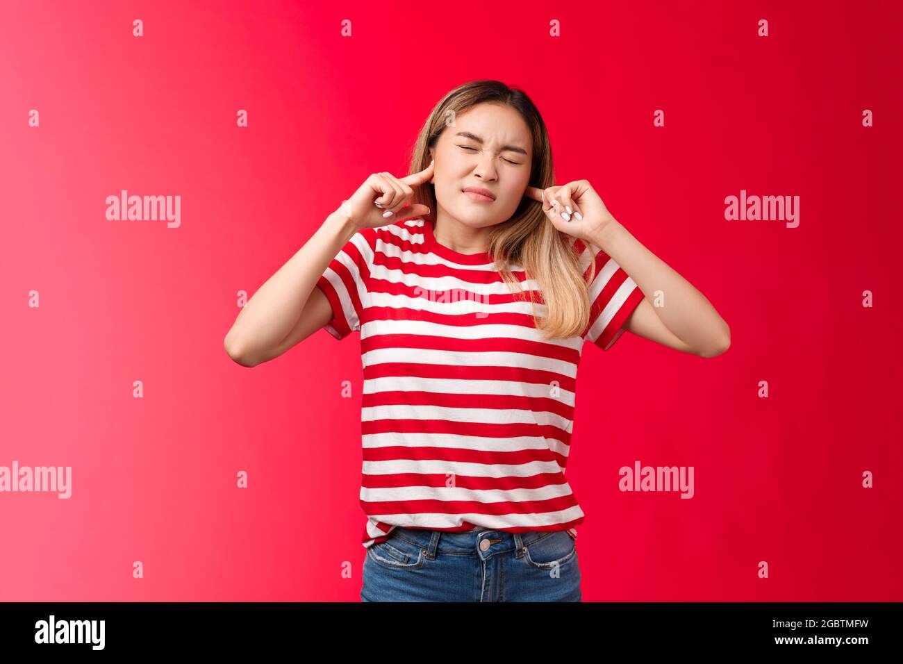 Gosh awful noise. Distracted and displeased blond korean girl grimacing ...