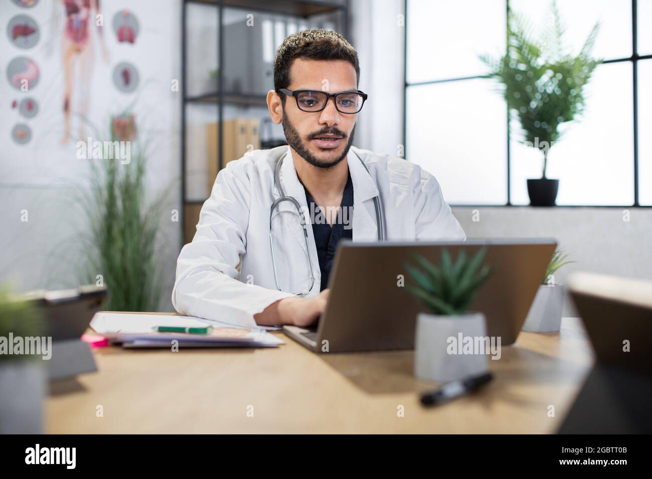 Telehealth concept. Young male Arabian doctor physician, looking at ...
