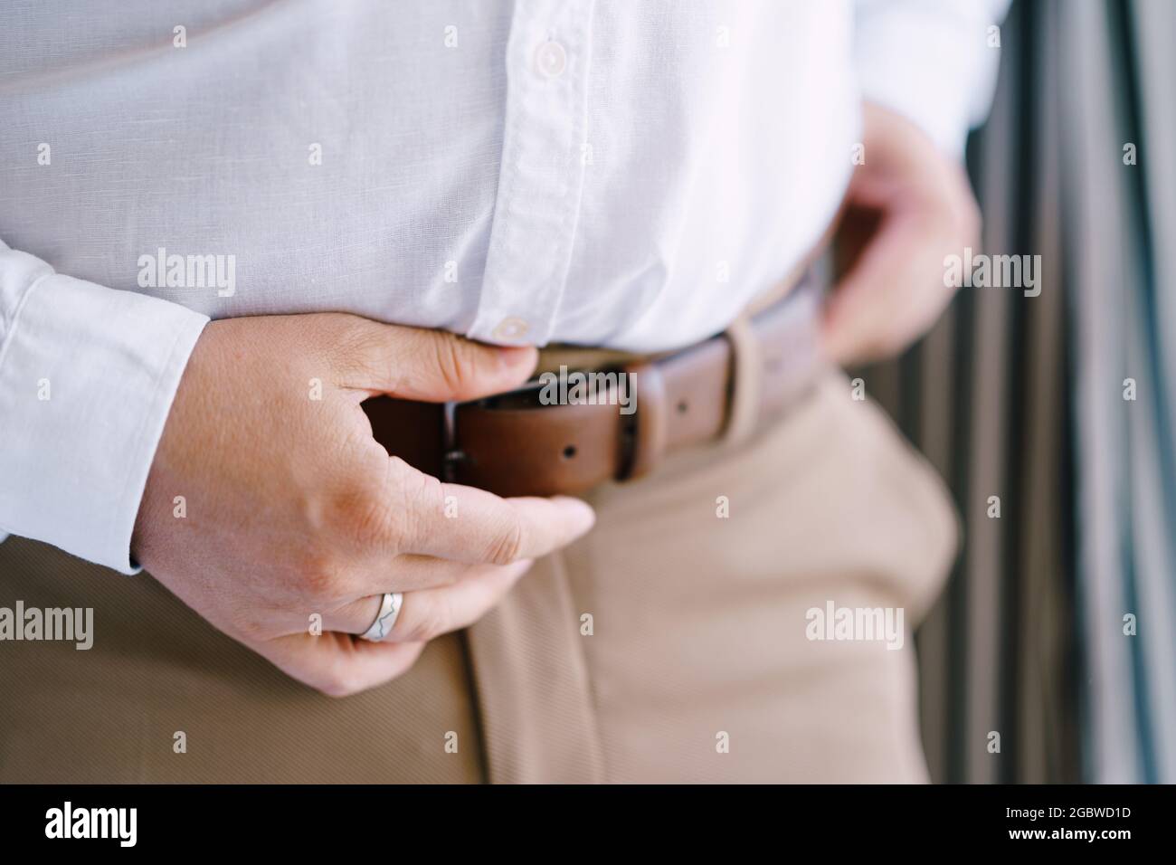Groom straightens the brown belt on his pants. Close-up Stock Photo - Alamy