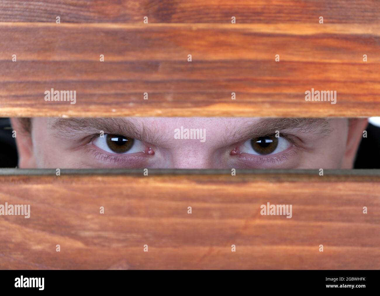 Man eyes looking through hole in wooden desk Stock Photo - Alamy