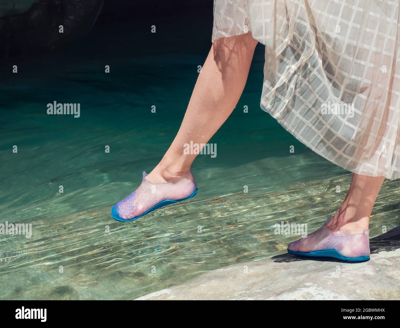 Female feet taking step into clear turquoise water outdoors under sun ...