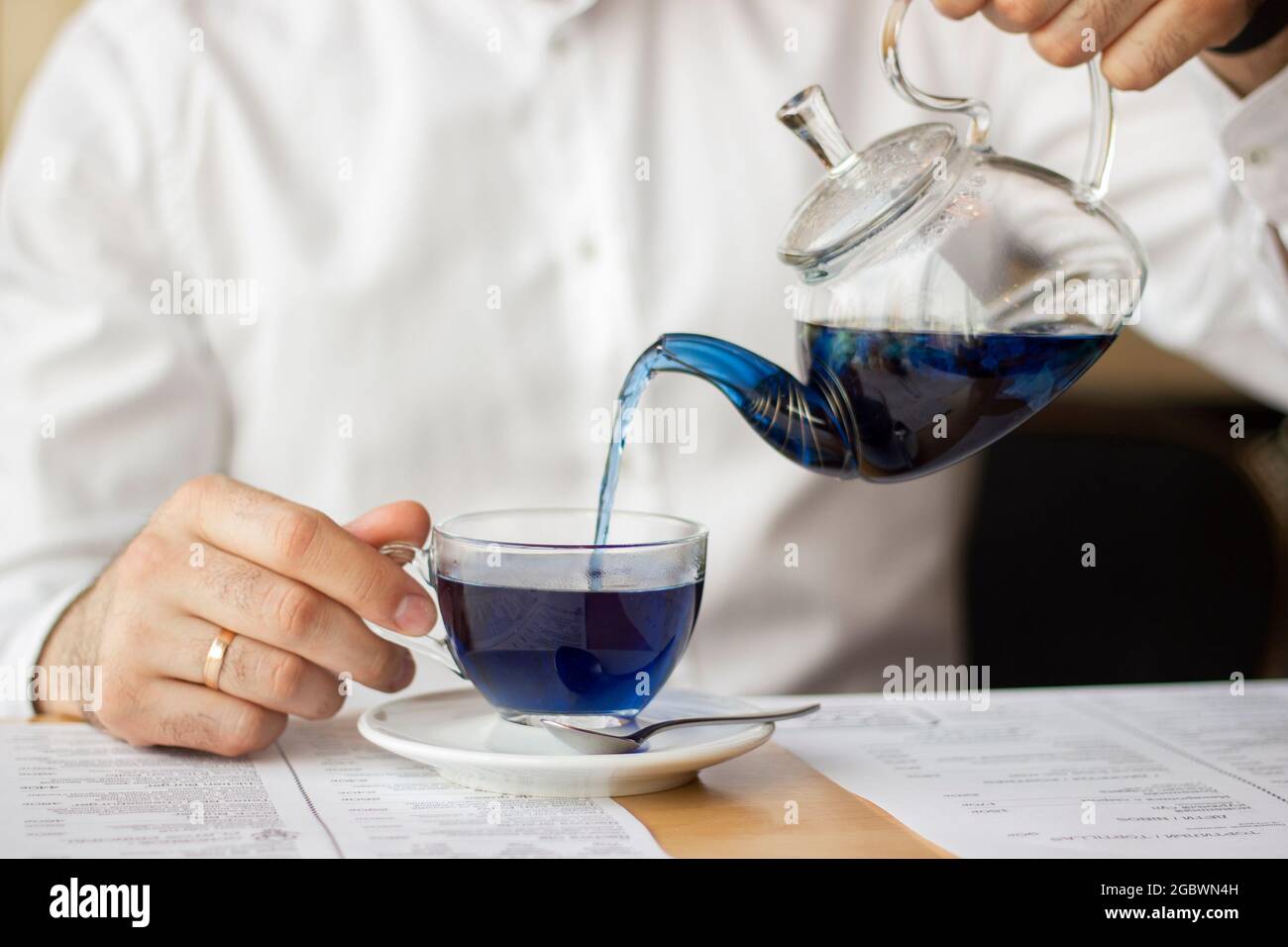 A man in a white shirt pours blue Chinese tea from a transparent teapot ...