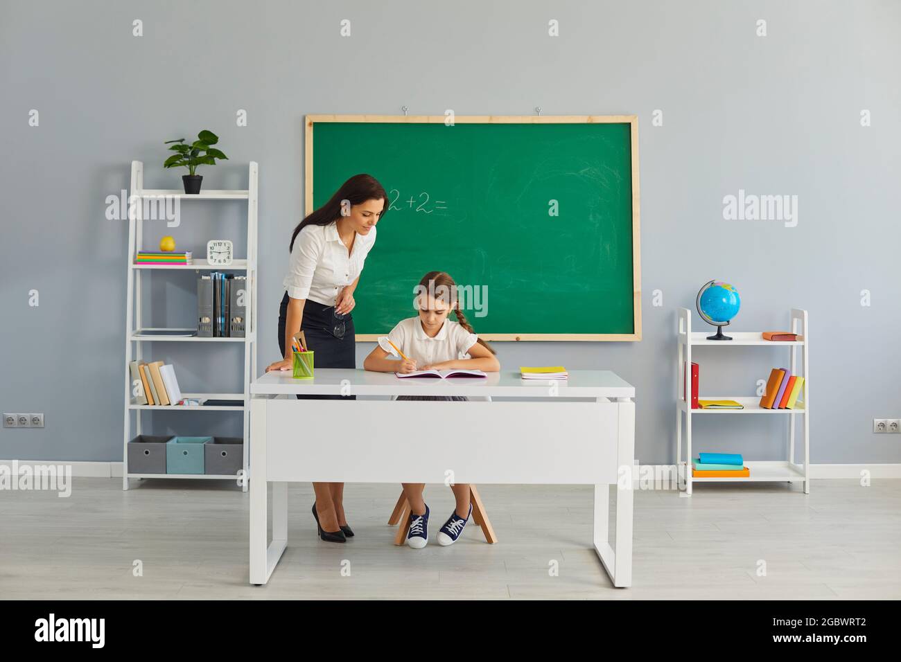 Friendly school teacher helping little pupil with math assignment in ...