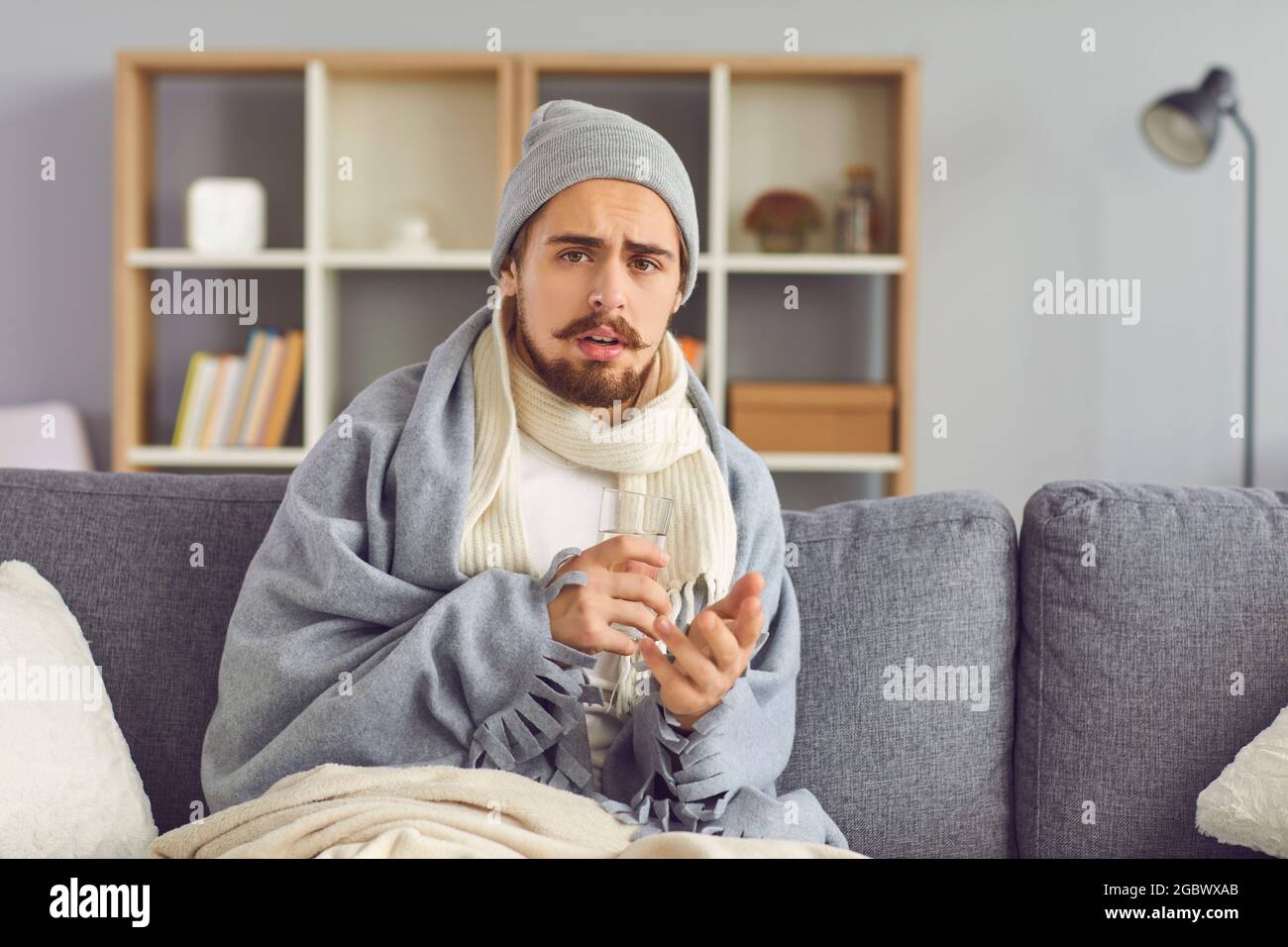 Young sick man in warm clothes sitting with glass of water and ...