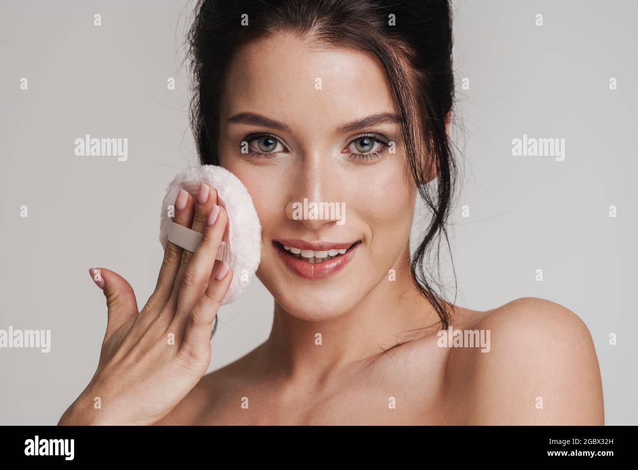 Young smiling white woman with brown hair pulled up holding powder puff ...