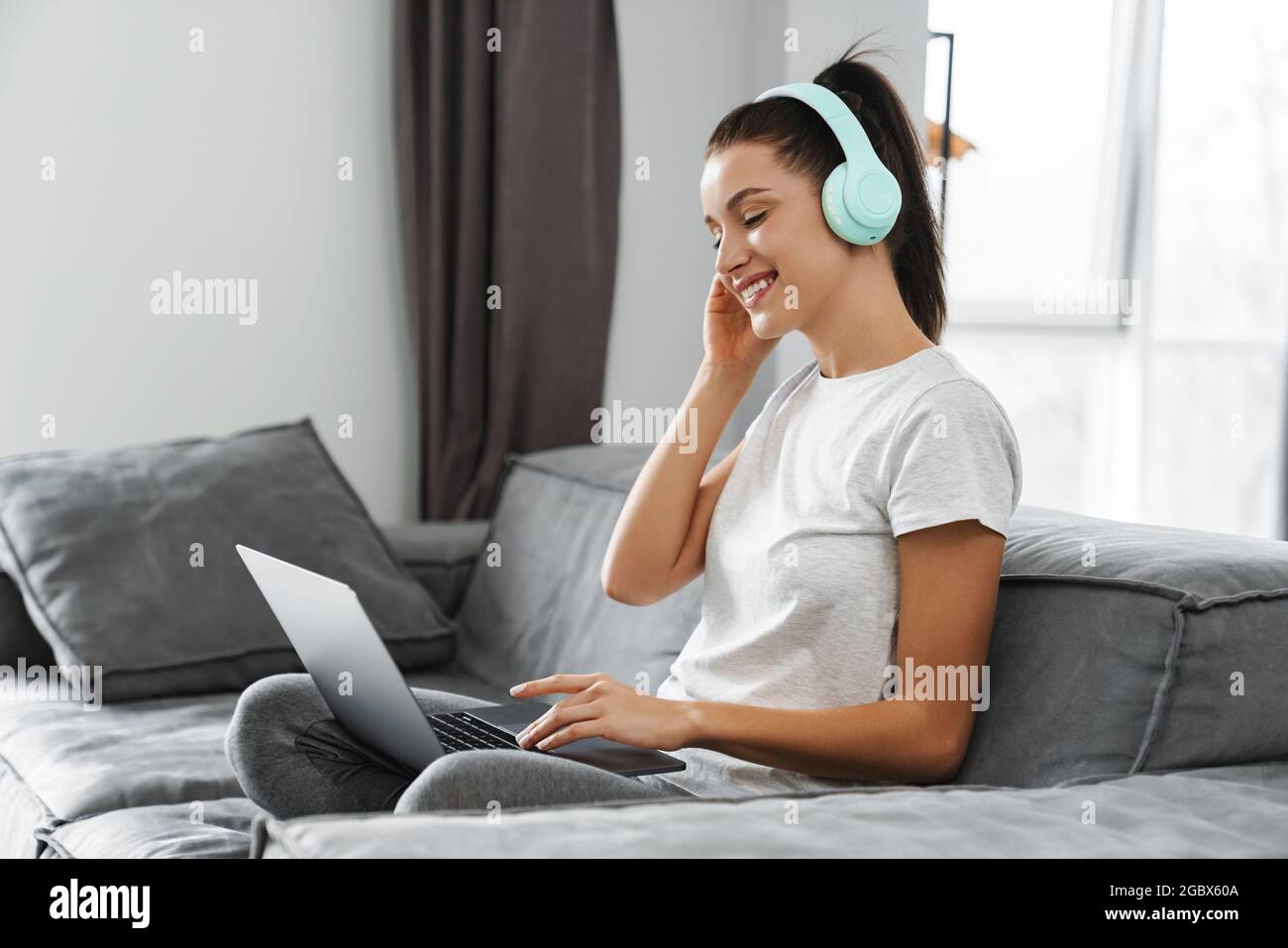 European smiling woman using headphones and laptop while sitting on ...