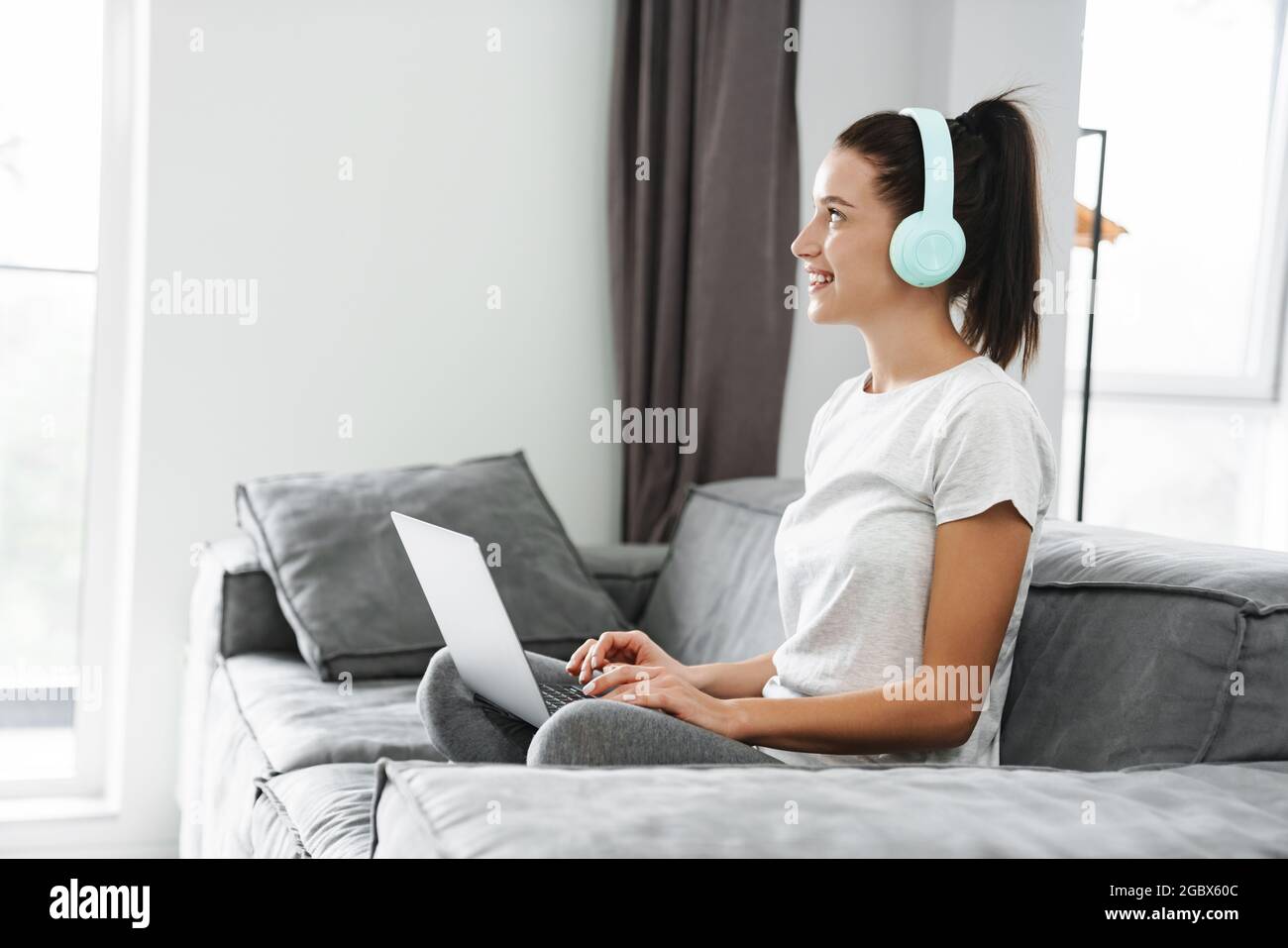 European smiling woman using headphones and laptop while sitting on ...