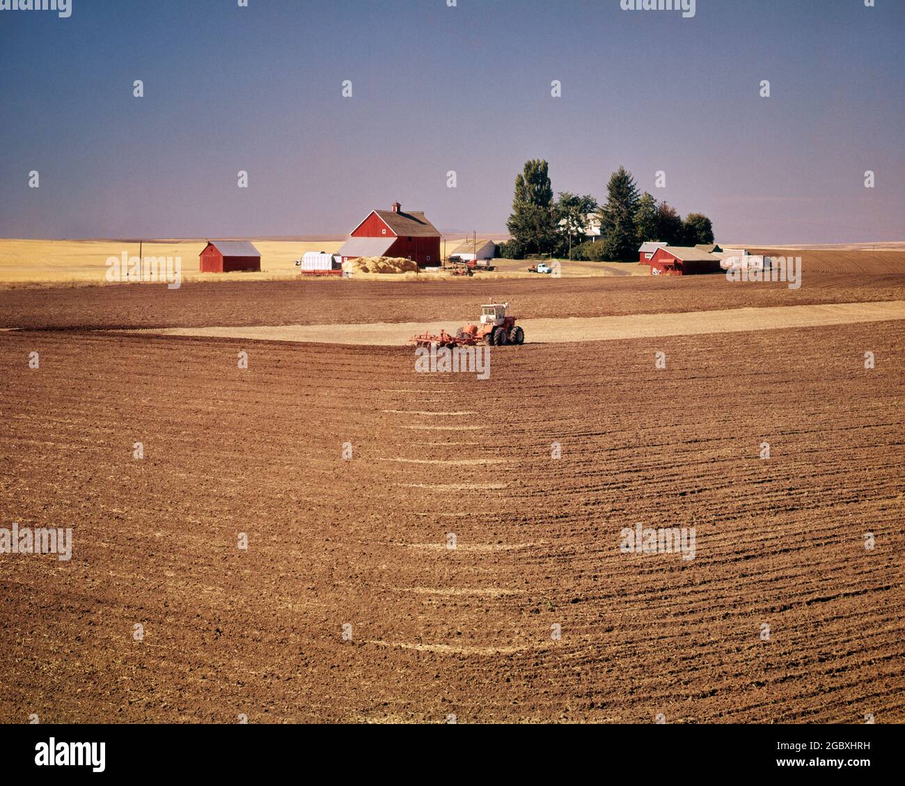 1980s TRACTOR PLOWING FIELD WITH FARM BUILDINGS IN BACKGROUND EASTERN ...