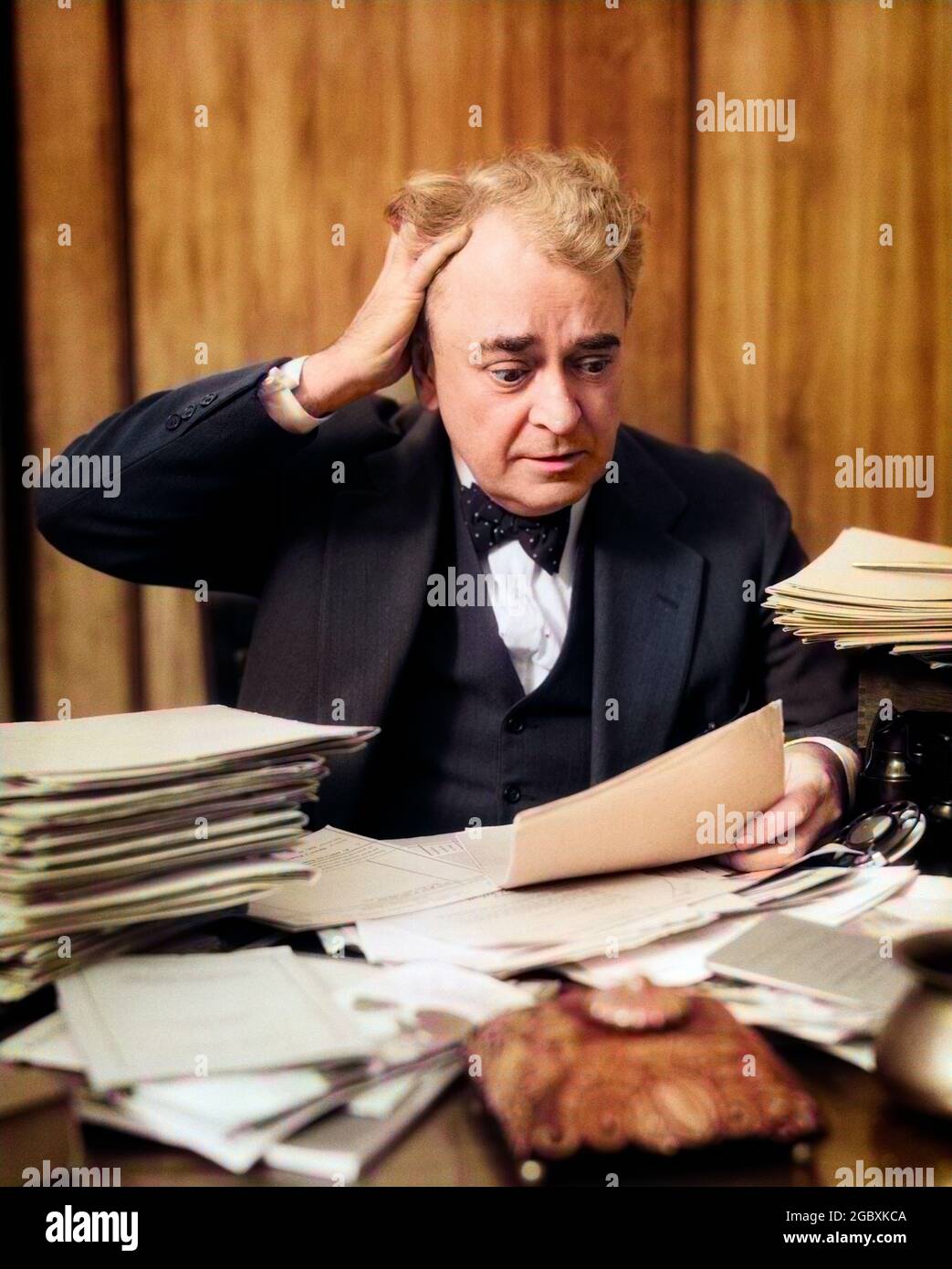 1930s ELDERLY BUSINESSMAN SITTING AT DESK AMONG STACKS OF PAPERS WITH ...