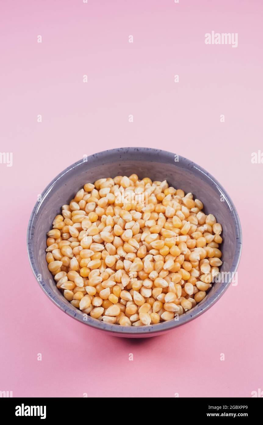 Vertical shot of corn grains on a bowl isolated on pink background ...