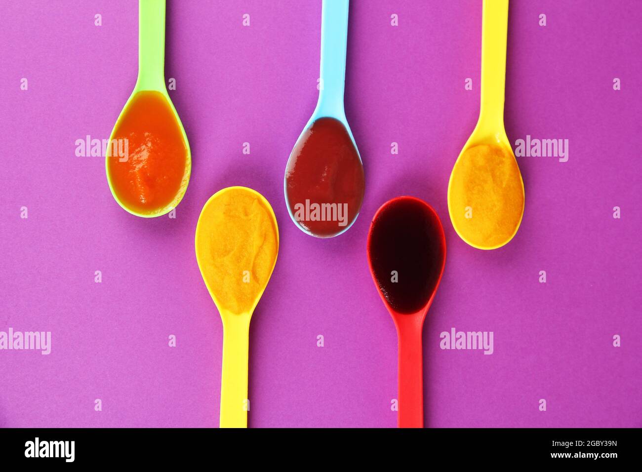 Baby puree in spoons on purple background Stock Photo - Alamy