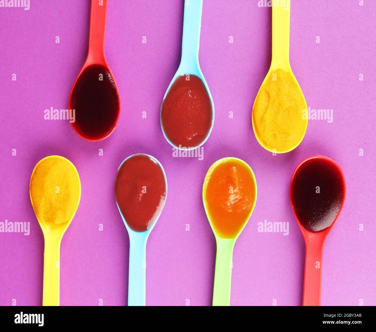 Baby puree in spoons on purple background Stock Photo - Alamy