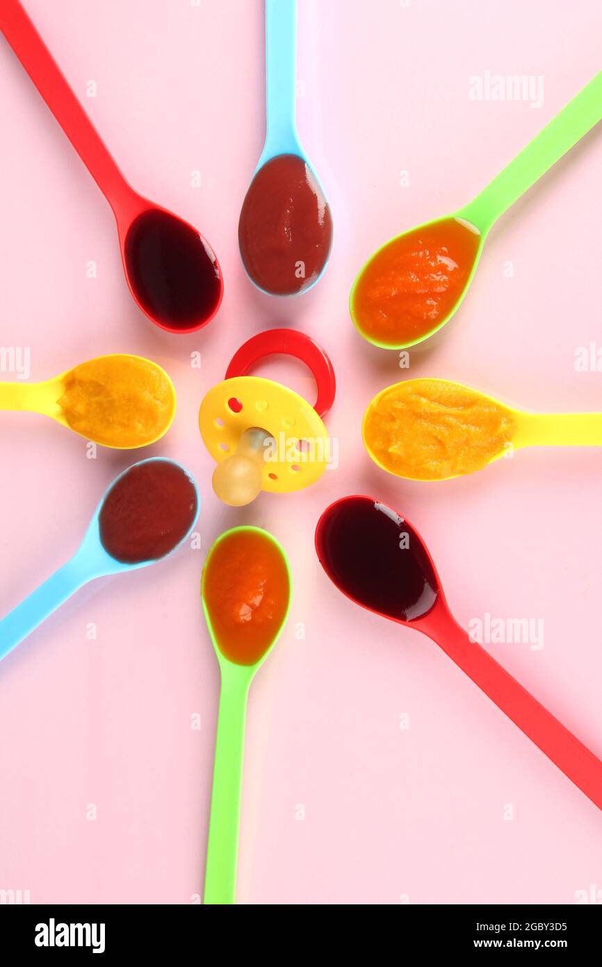 Baby puree in spoons with nipple on pink background Stock Photo - Alamy