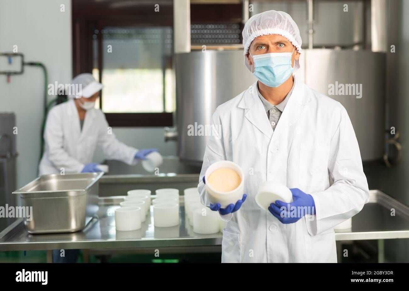 Cheesemaker in protective mask working in shaping workshop of cheese ...