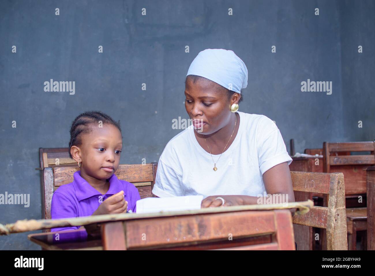 African Nigerian mother or teacher sitting together with her girl child ...