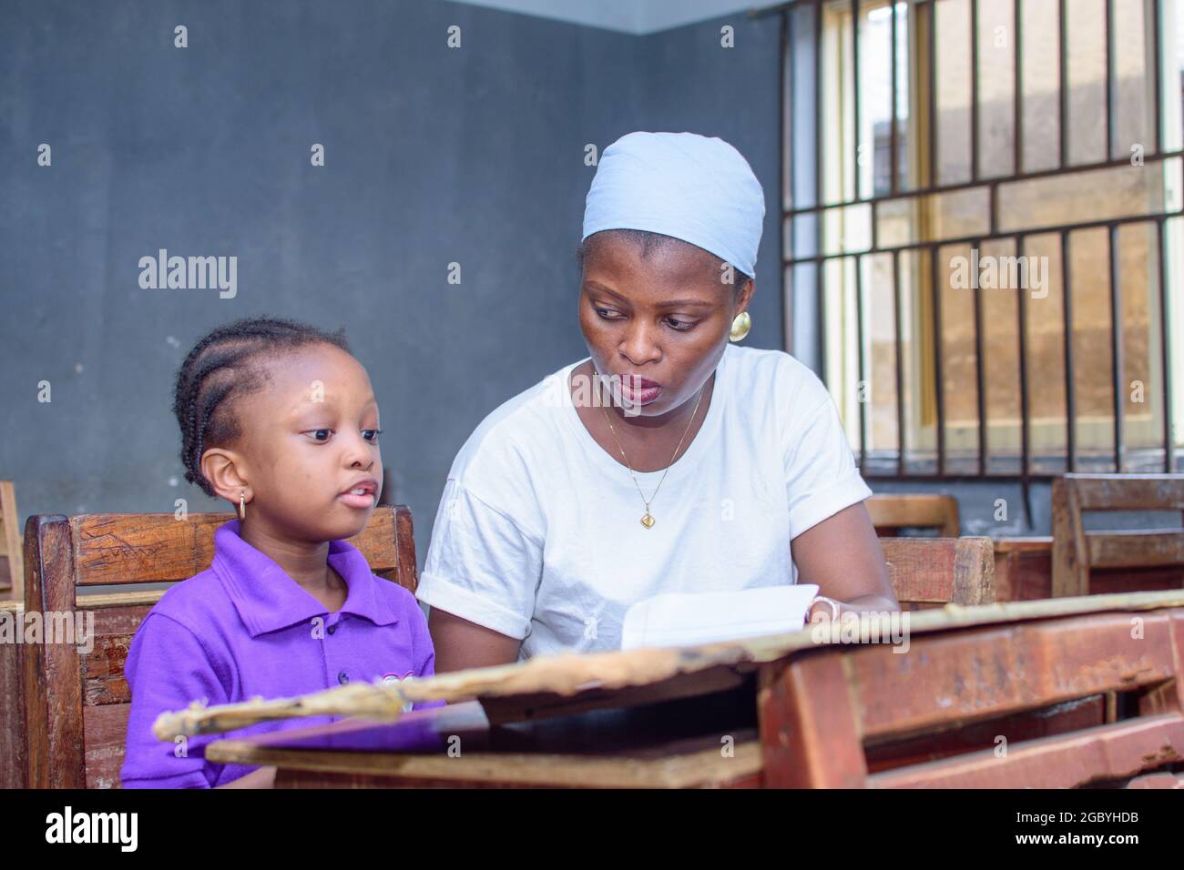 African Nigerian mother or teacher sitting together with her girl child ...