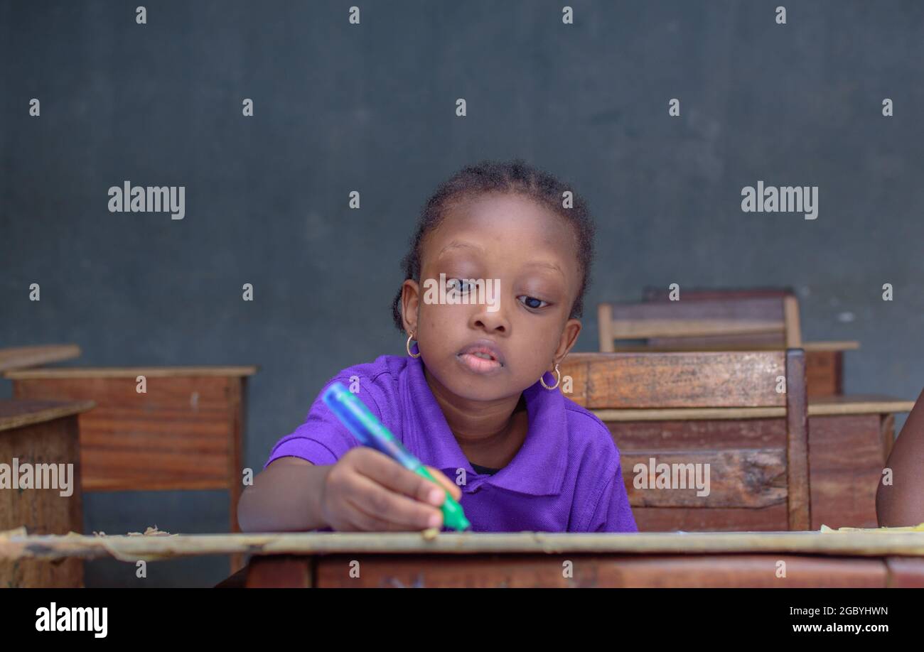 African girl child, pupil or student sitting down and writing in a ...