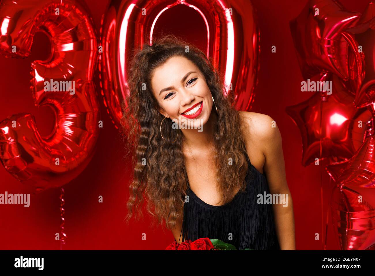 Portrait of happy 30 year old woman on red background with red balloons ...